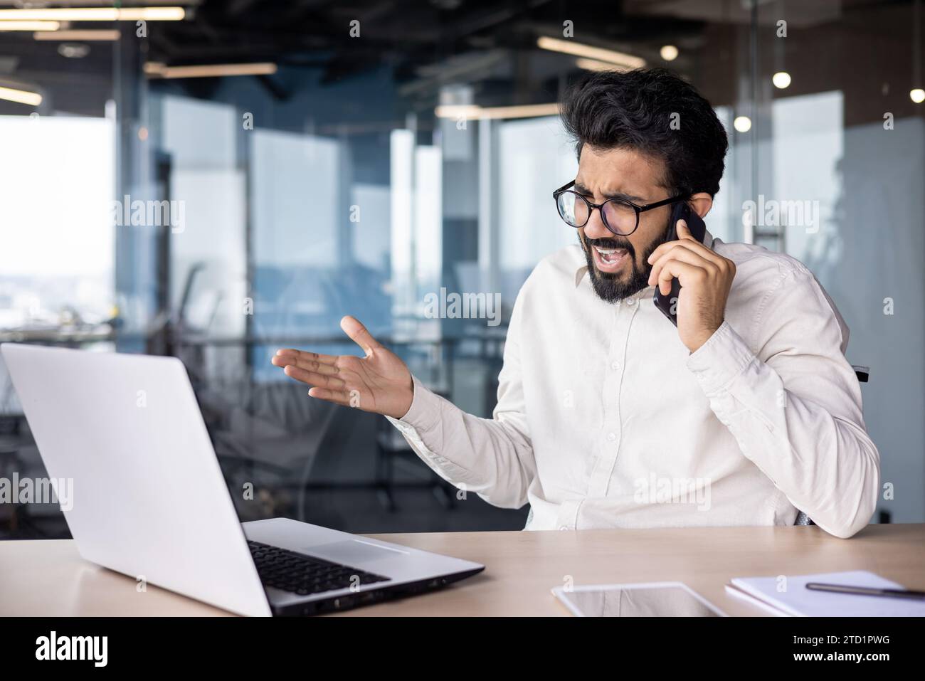 Angry young Indian male businessman sitting in the office at the desk ...