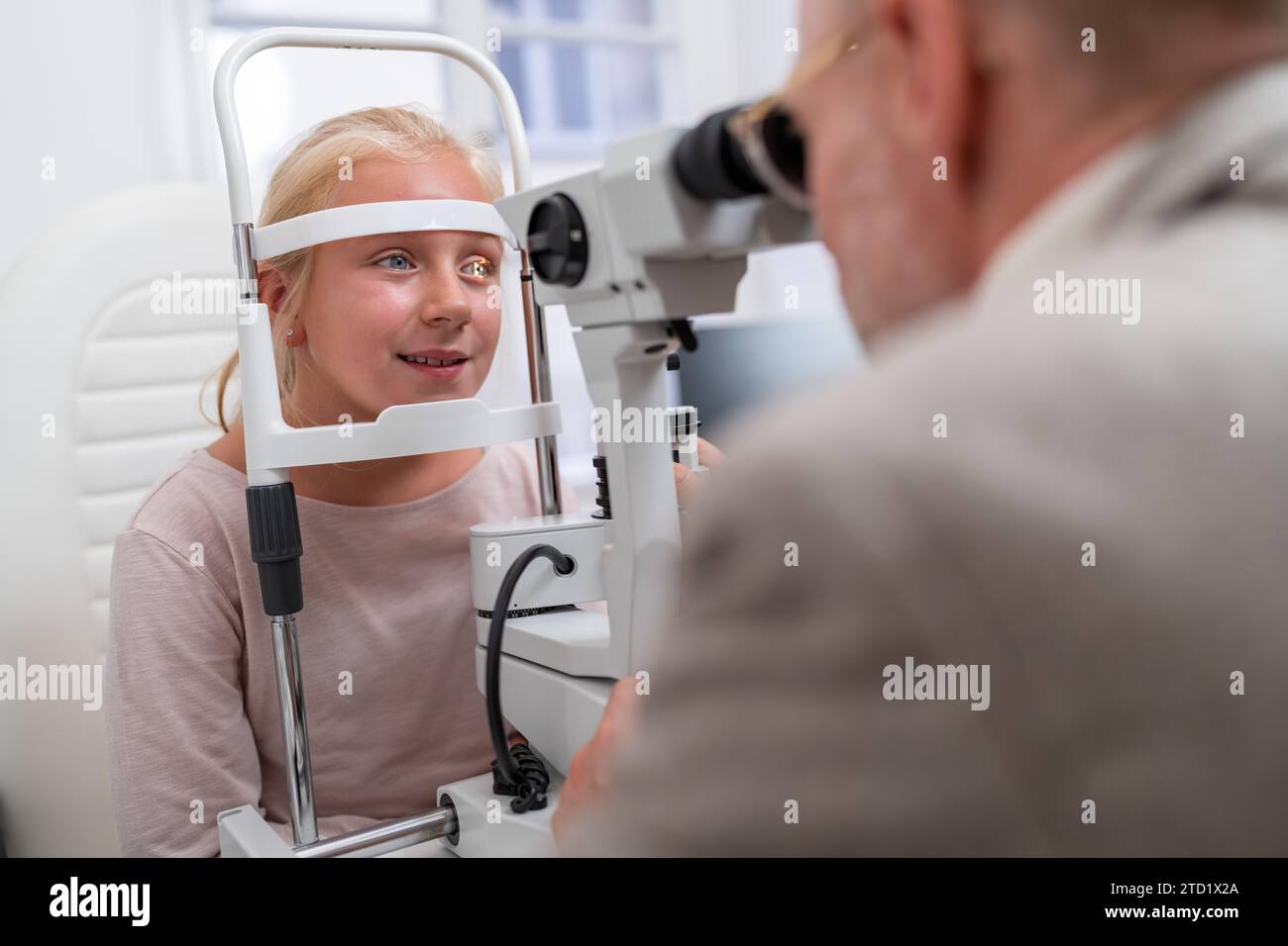 Eye examination with young girl looking into an optometry machine at ...