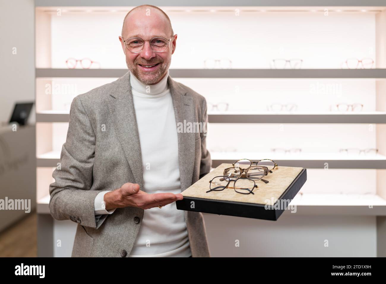 Happy optician presenting a tray with various eyeglasses at an optical ...
