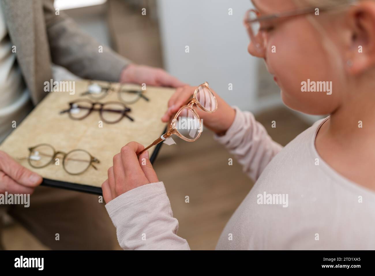 Girl trying on newglasses. She is looking at different frames on a tray ...