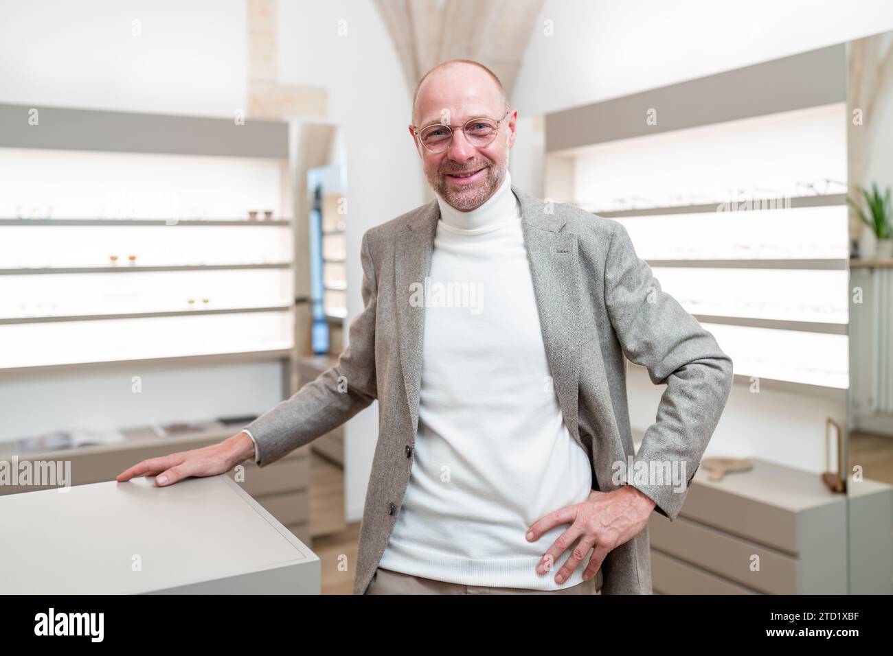 optician wearing glasses smiling in an eyewear shop. He is wearing a ...