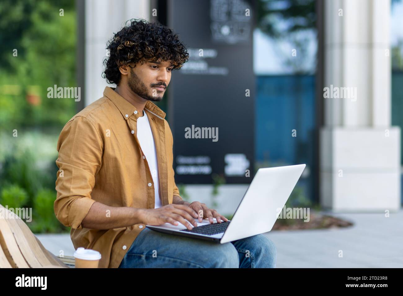Serious Indian young man working and studying outdoors, sitting on a ...
