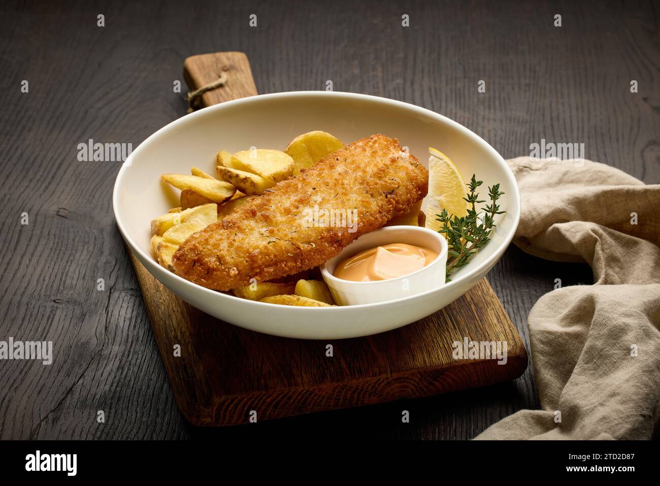 bowl of breaded fish fillet and fried potato wedges on dark wooden ...