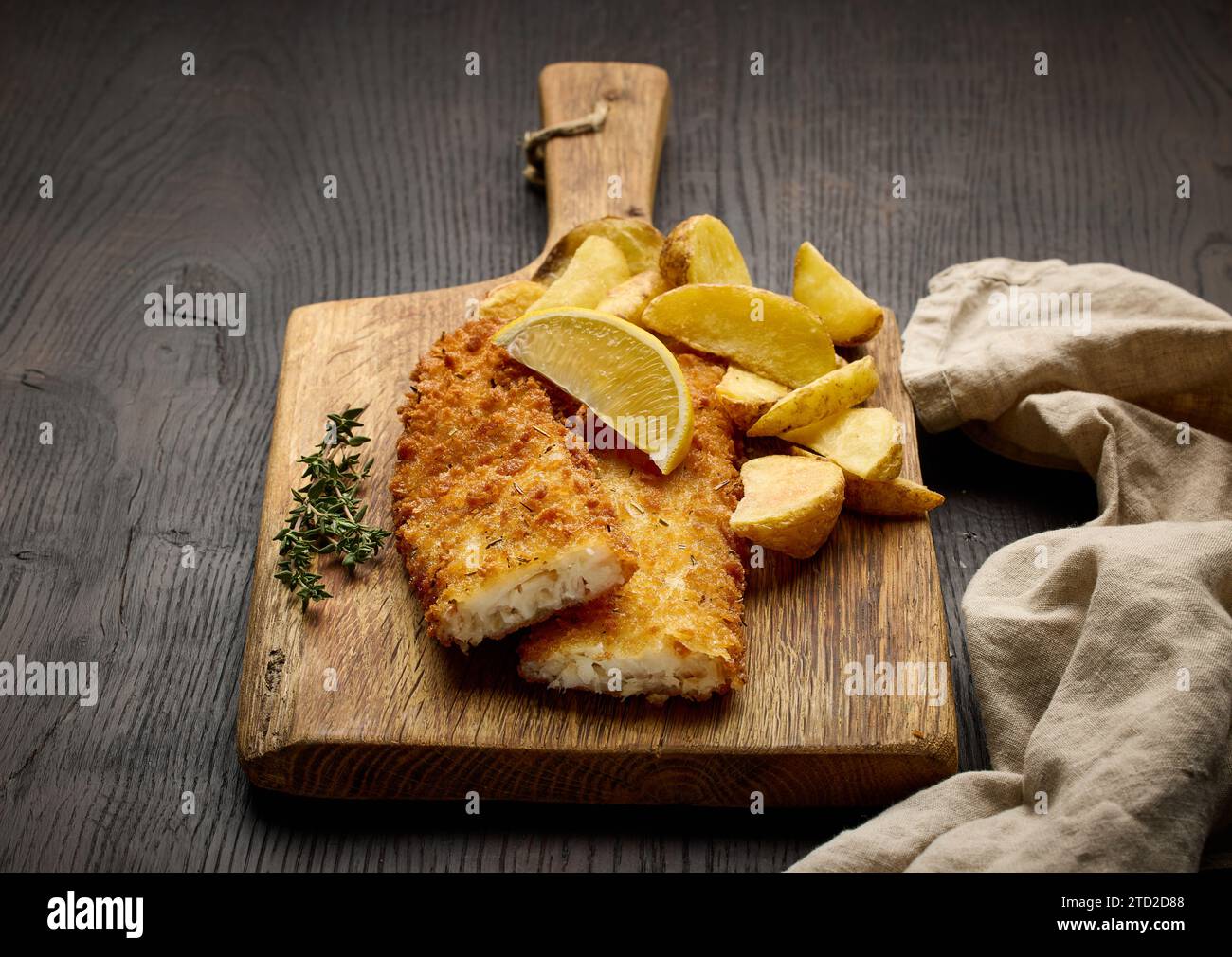 breaded fish fillets and fried potato wedges served on wooden cutting ...