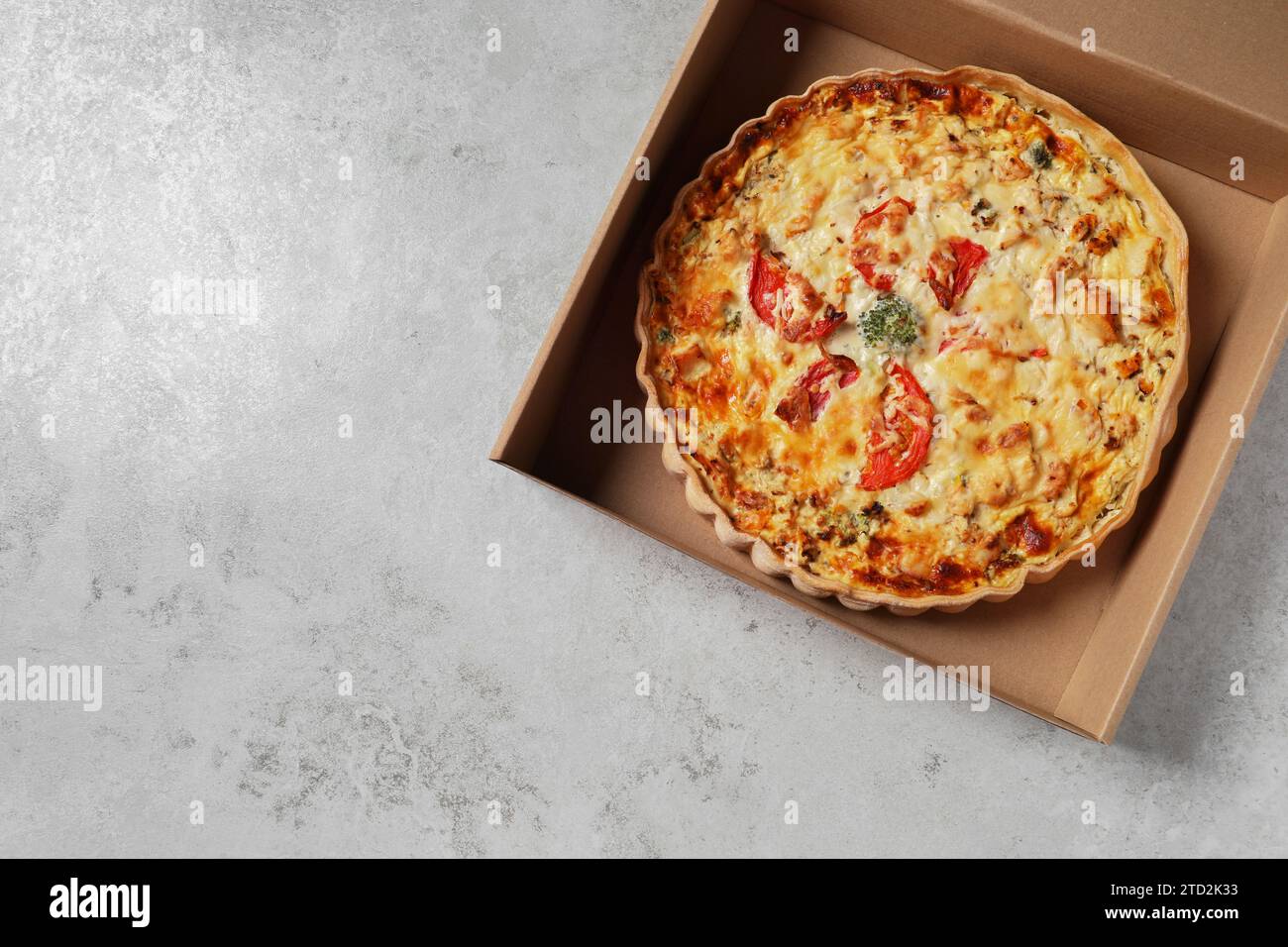 Tasty quiche with tomatoes and cheese in open box on light table, top ...