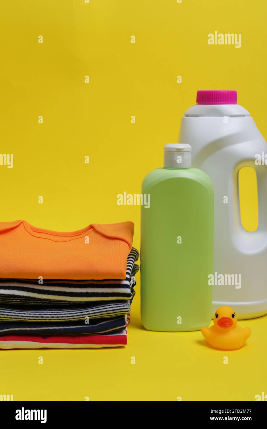 Laundry detergents, stack of baby clothes and rubber duck on yellow ...