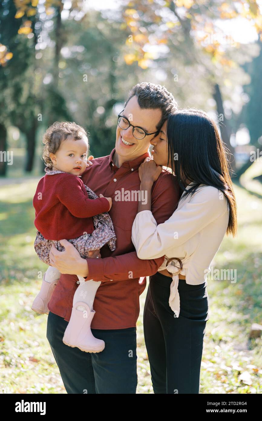 Mom hugs happy dad with a little girl in his arms by the shoulders ...