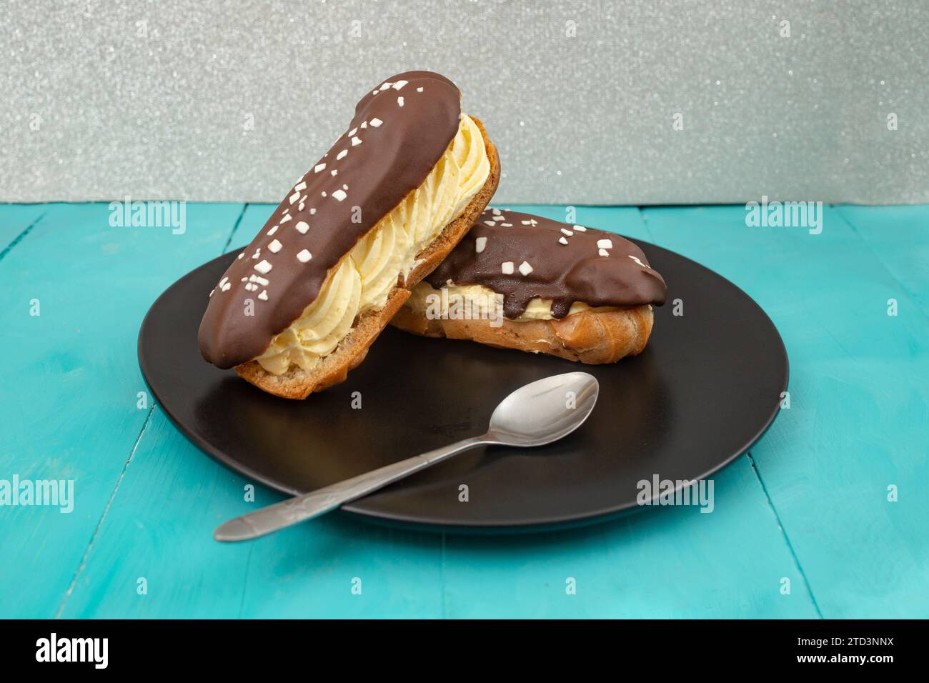 Two eclair cakes on a black ceramic plate, and blue wooden boards table ...
