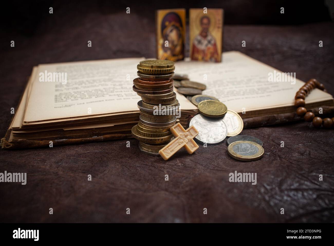 Stack of coins, opened bible and a small crucifix on leather desk ...
