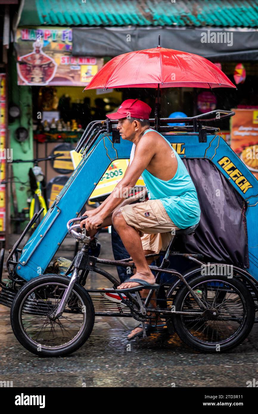 A filipino tuk tuk or trike driver makes his way into the busy streets ...