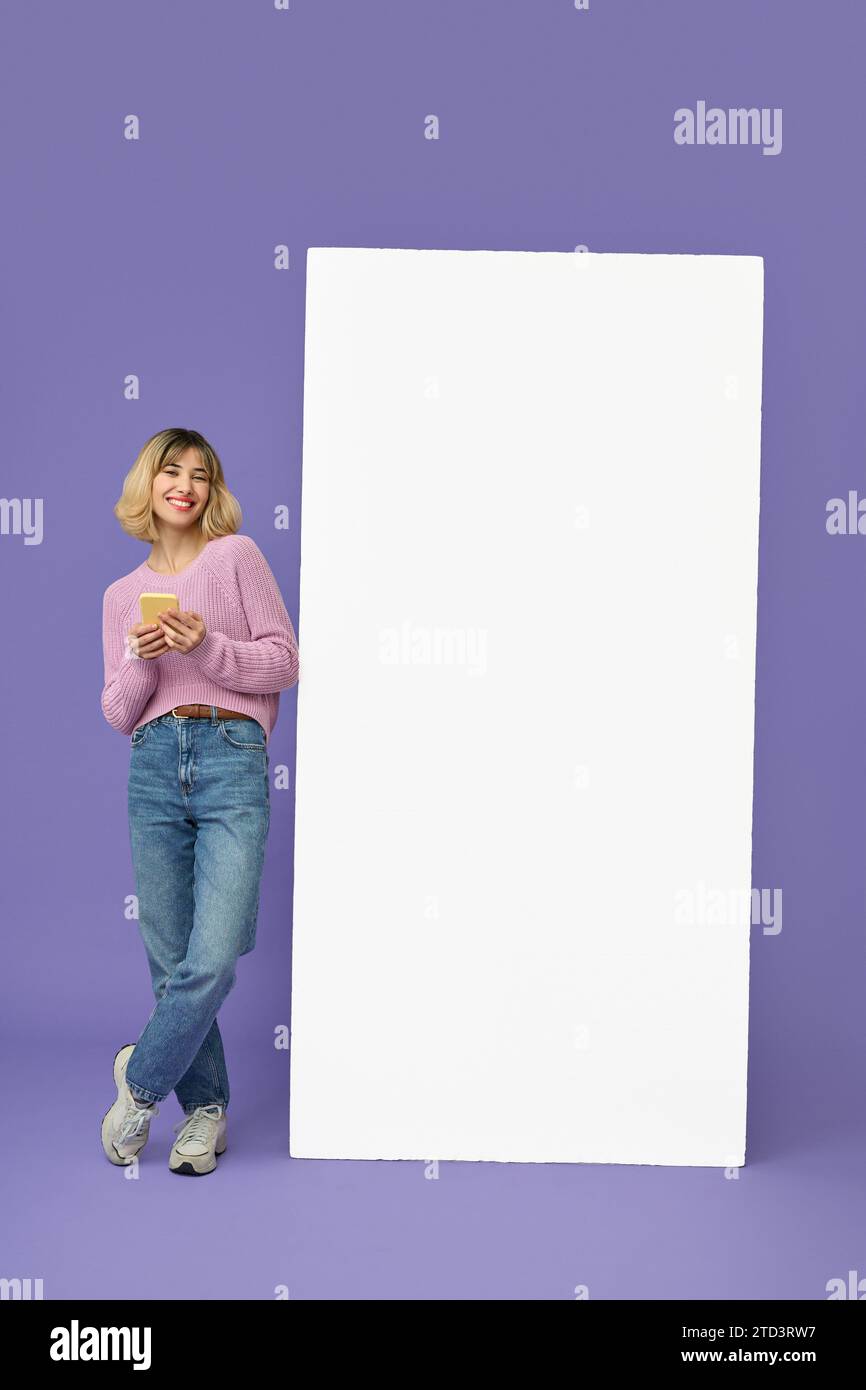 Happy gen z girl using cellphone standing near big phone mockup screen ...
