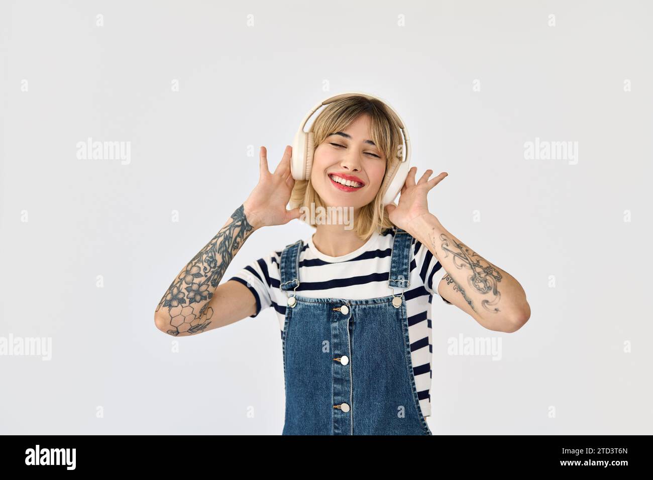 Happy gen z girl with tattoos in headphones listening music isolated on ...