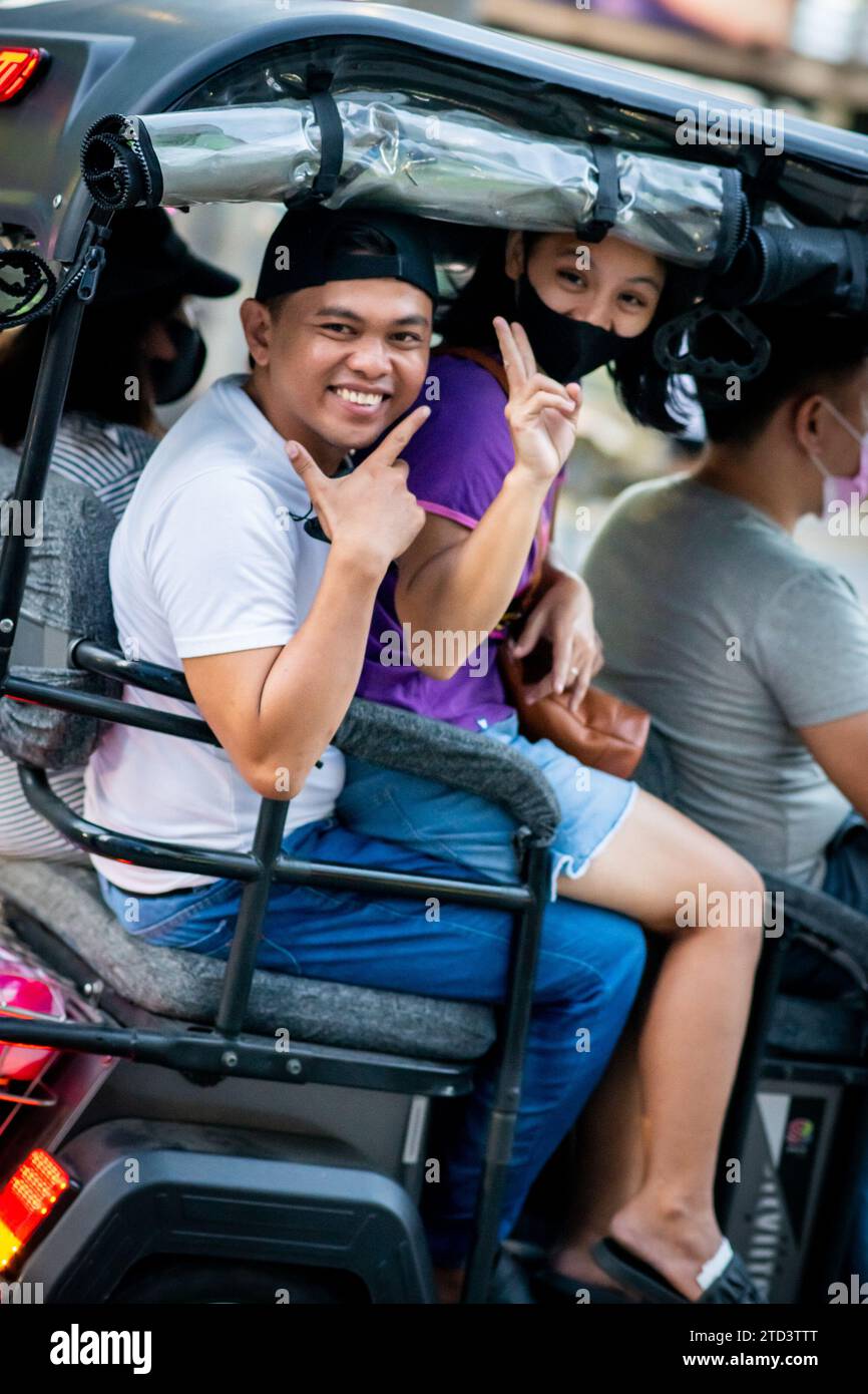 A Young happy Filipino couple on a tuk tuk smile and give the thumbs up ...