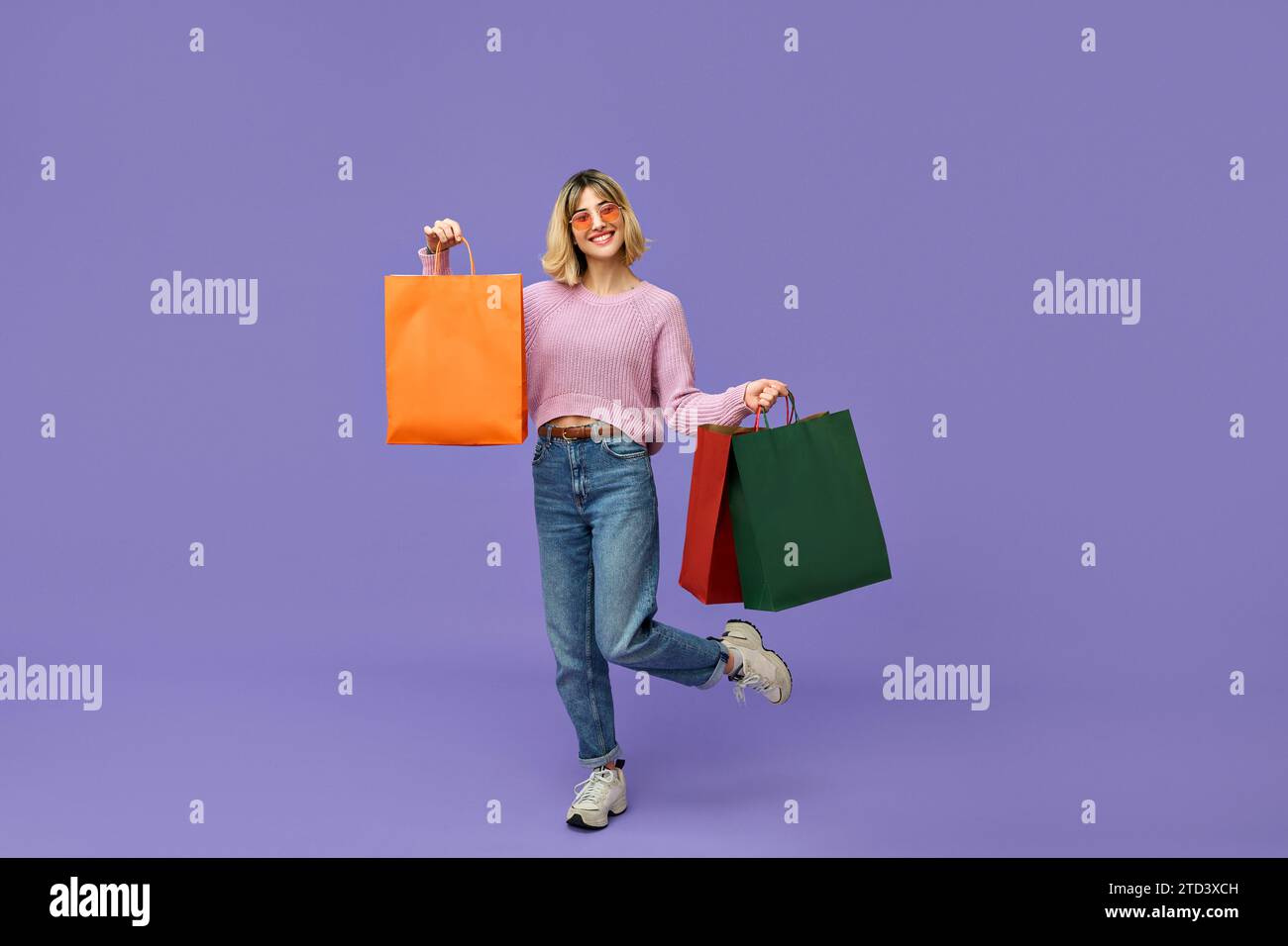 Happy gen z blonde young woman holding shopping bags isolated on purple ...