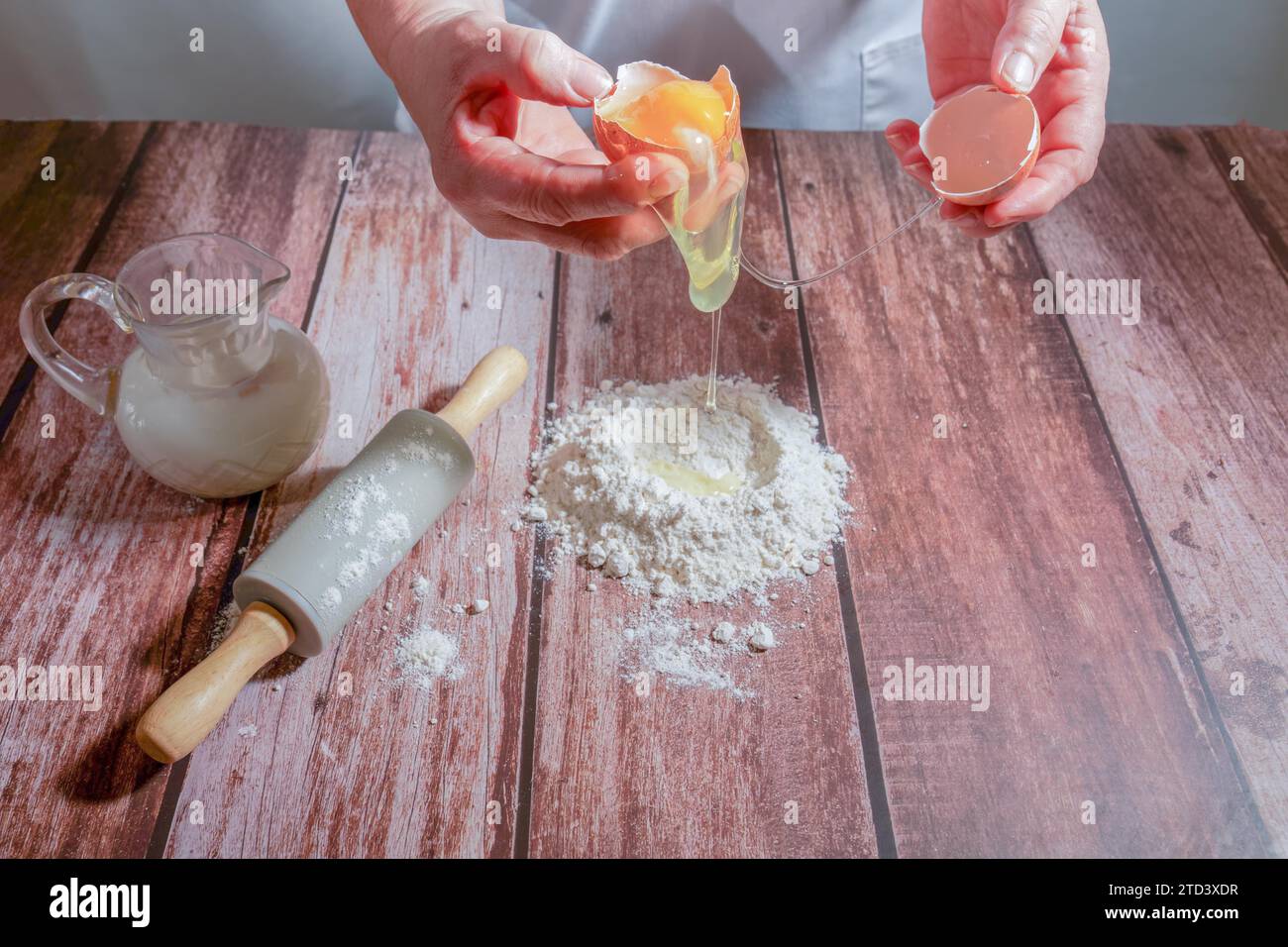 Woman breaking an egg, pouring it over flour to make a sponge cake on a ...