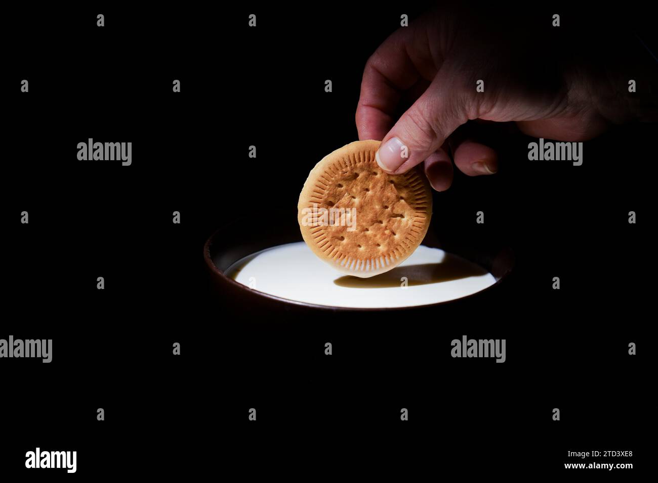 Woman's hand dipping a cookie in a bowl of milk isolated on a black ...