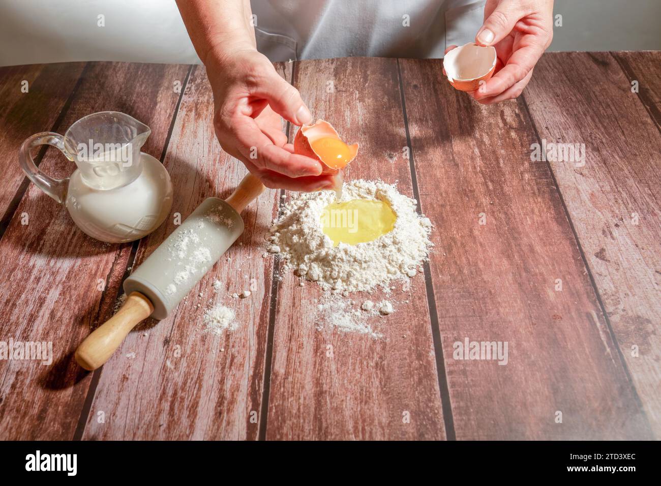 Woman breaking an egg, pouring it over flour to make a sponge cake on a ...