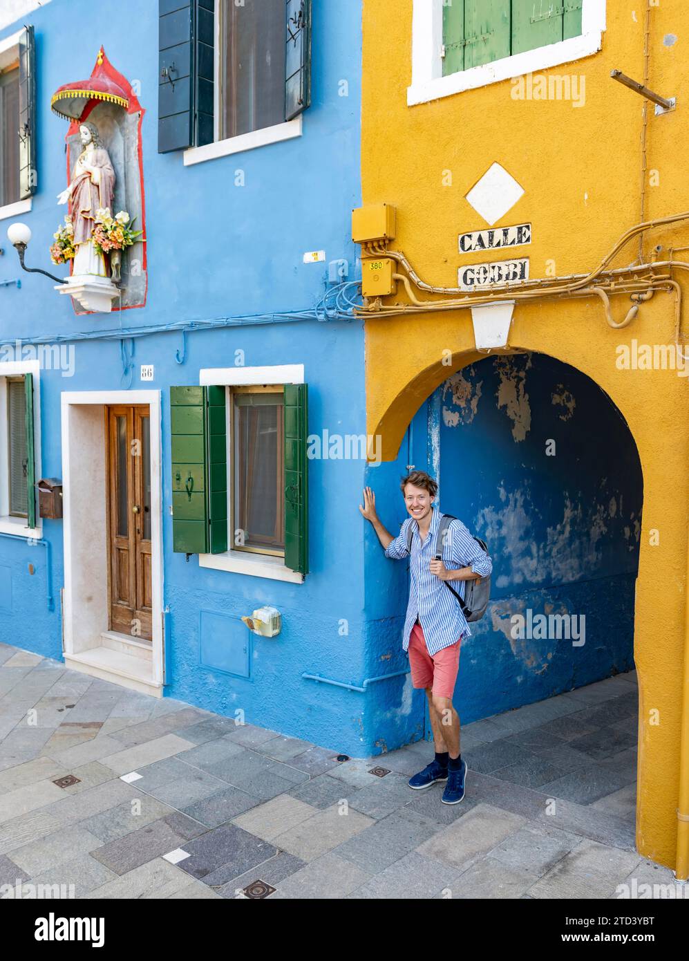 Young man with backpack in a passageway, blue and yellow house facade ...