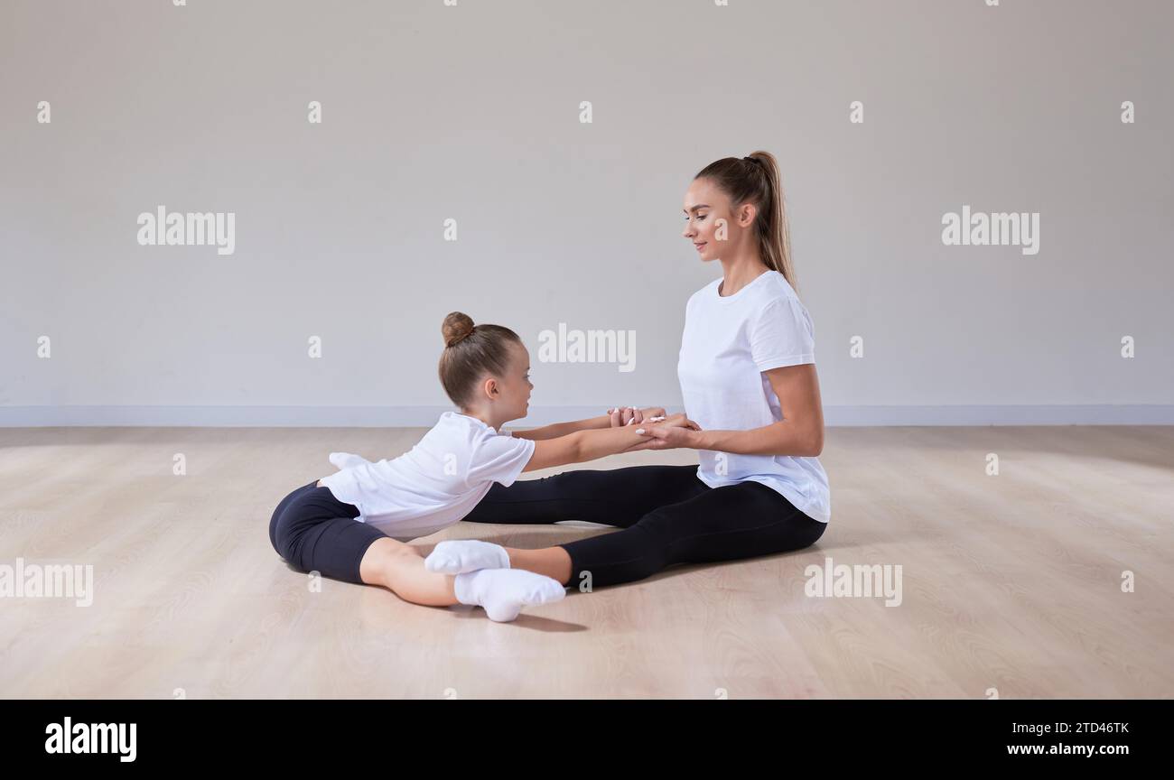 Beautiful female teacher helps a little girl stretch in a gymnastics ...