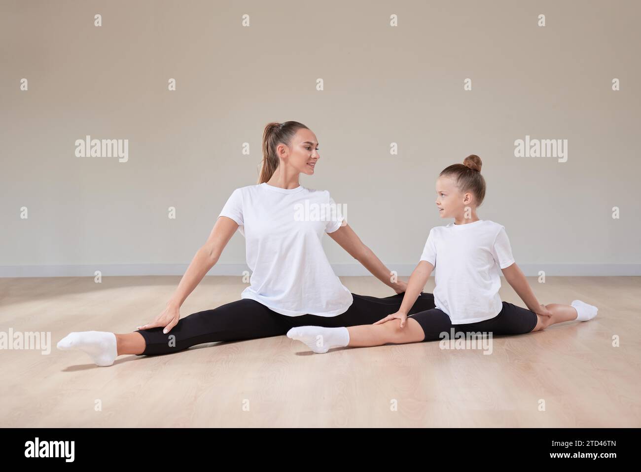 Beautiful female teacher and a little girl are sitting in the splits in ...
