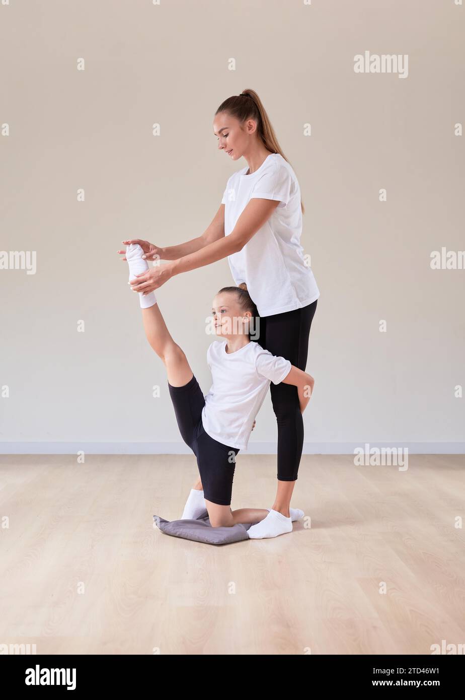 Beautiful female teacher helps a little girl stretch in a gymnastics ...