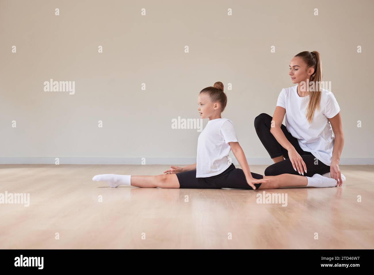 Beautiful female teacher helps a little girl stretch in a gymnastics ...