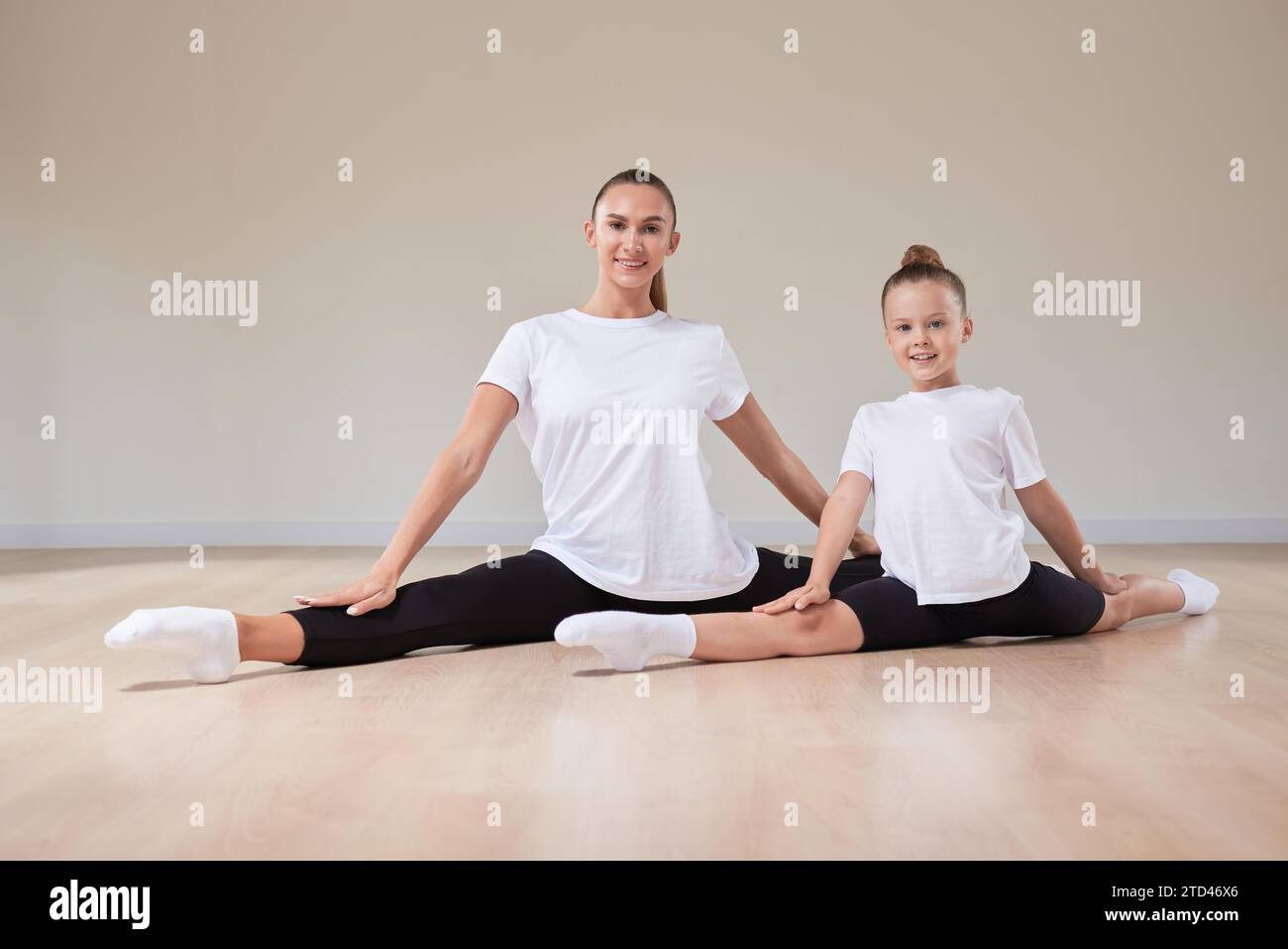 Beautiful female teacher and a little girl are sitting in the splits in ...