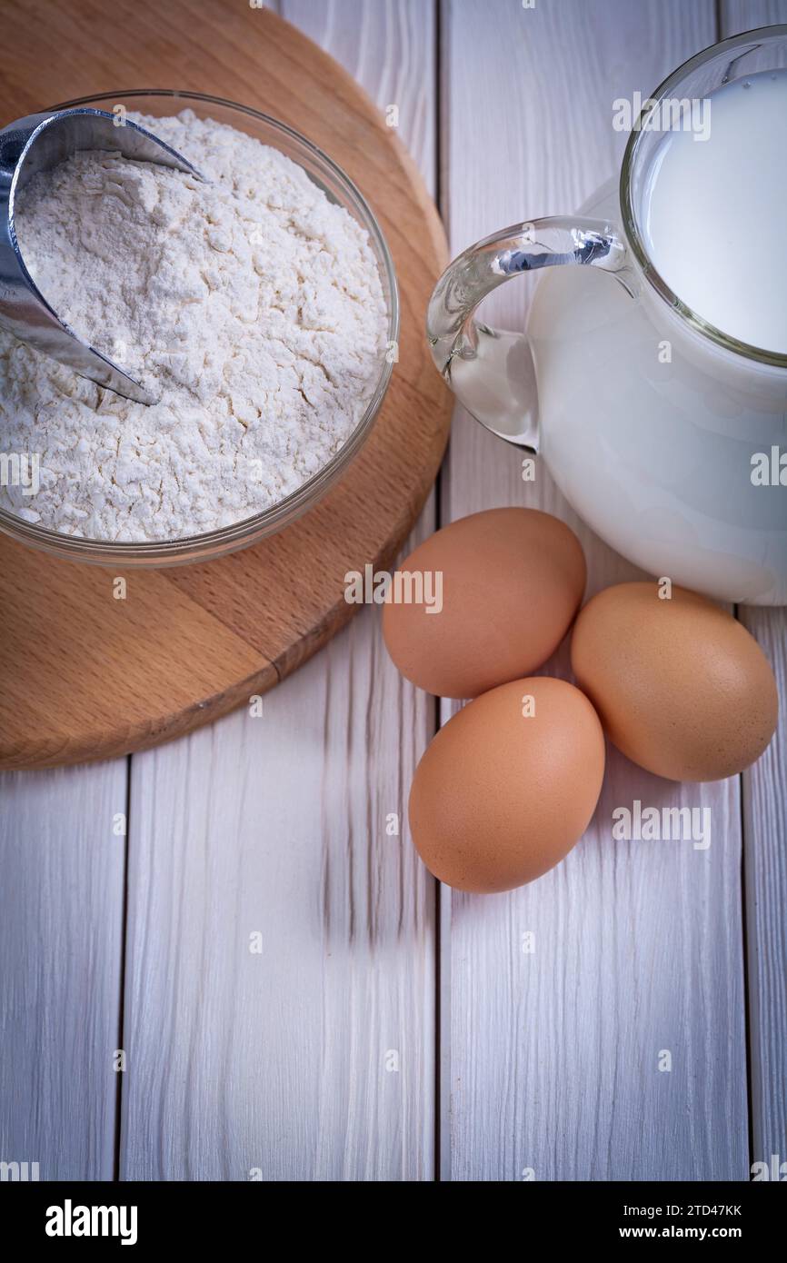 Aerial view flour in bowl scoop eggs jug with milk on white lacquered ...