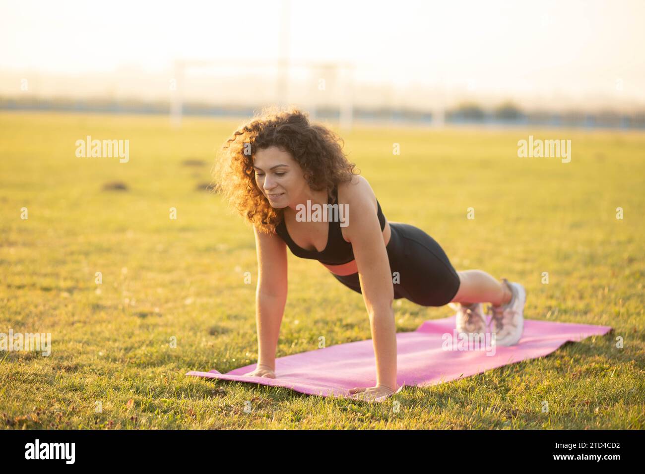 Curly girl runner doing plank exercise on a yoga mat on the lawn Stock ...