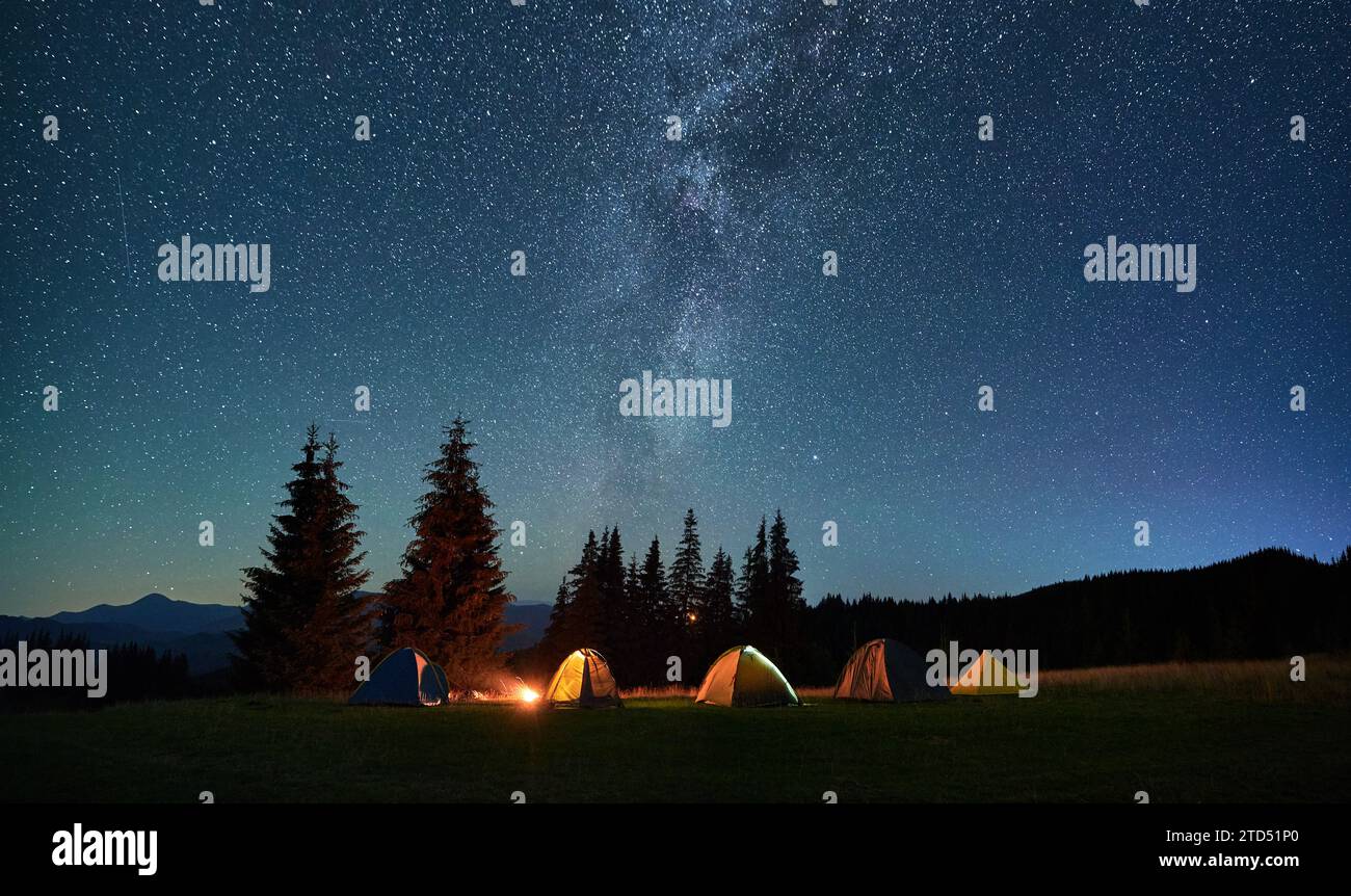 Night camping in mountains under starry sky. Tourist tents in campsite near burning campfire ...