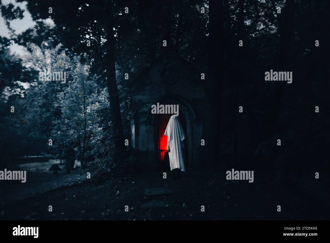 At night, a creepy ghost stands in the cemetery among the trees near ...