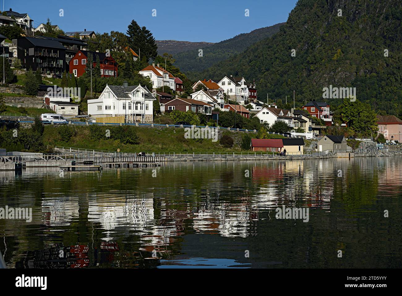 Colorful buildings along the hill side and their reflections on the lake in Sogndal, Norway ...