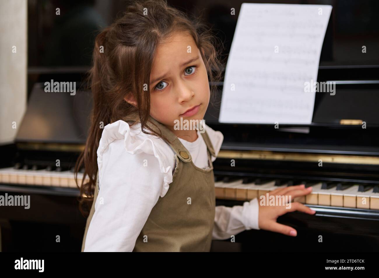 Authentic child girl looking at the camera, sitting at grand piano ...