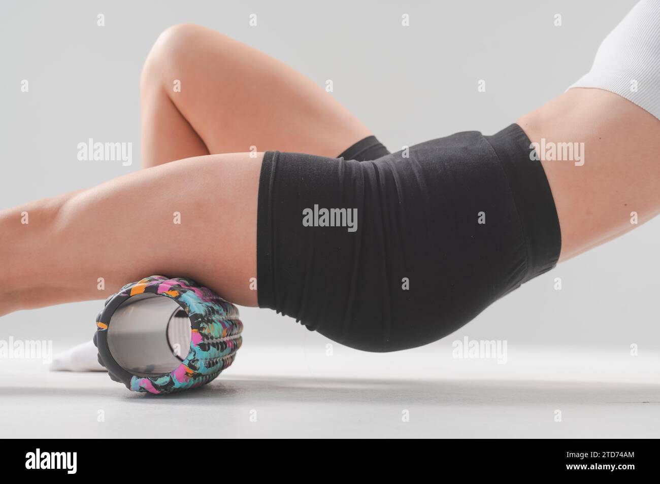 Faceless woman doing roller exercise for myofascial release on white ...