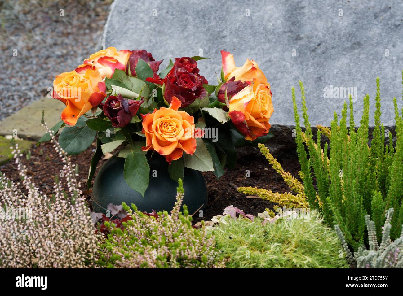 a black round vase with red and orange roses on a grave with an ...