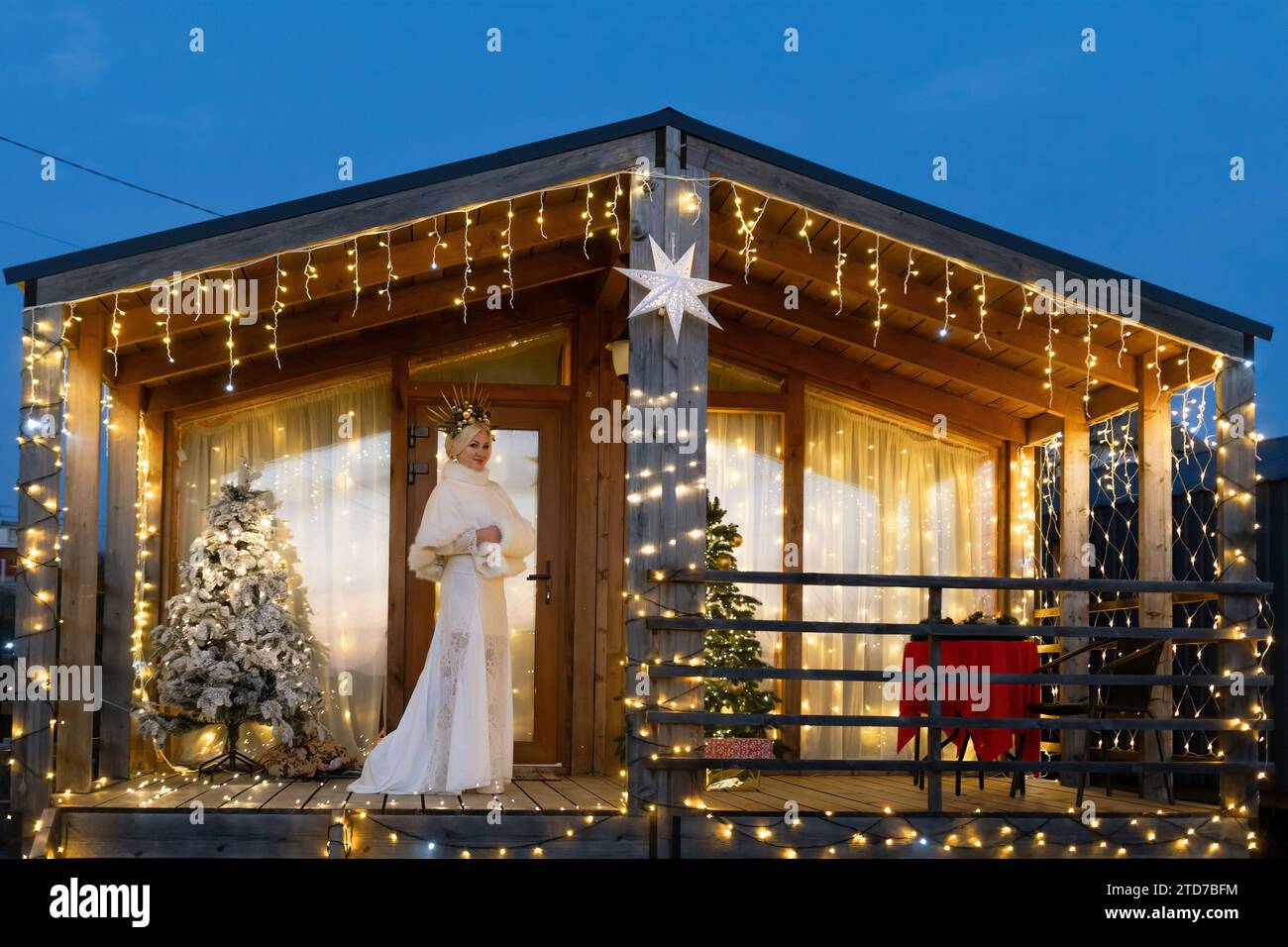 Happy blonde as Snow Maiden in white costume. Wooden house exterior ...
