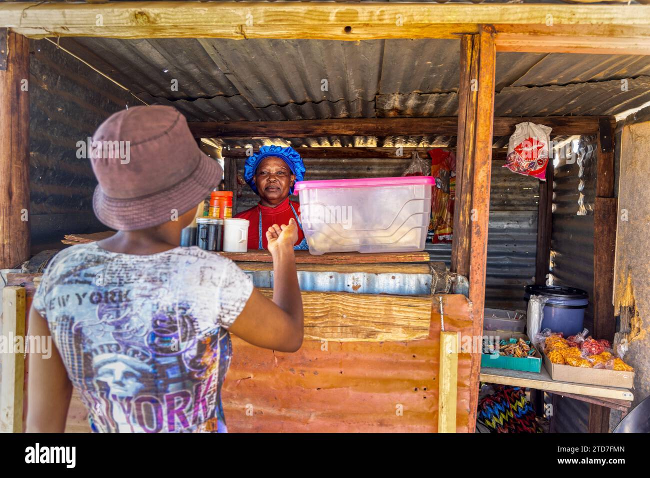 street vendor in a shack, selling to a young african woman, some snacks ...