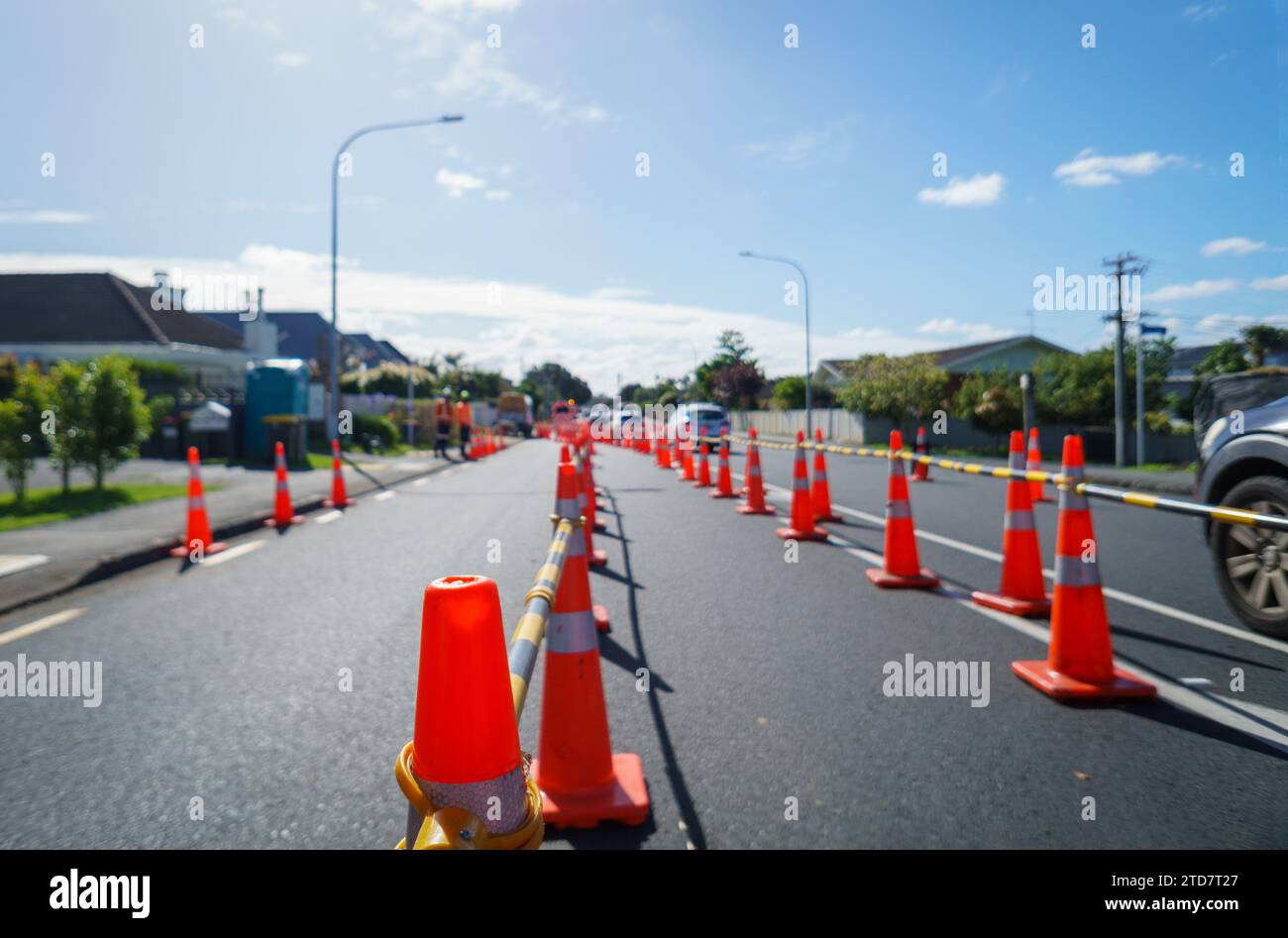 Orange traffic cones lining up the street. Unrecognizable workers ...