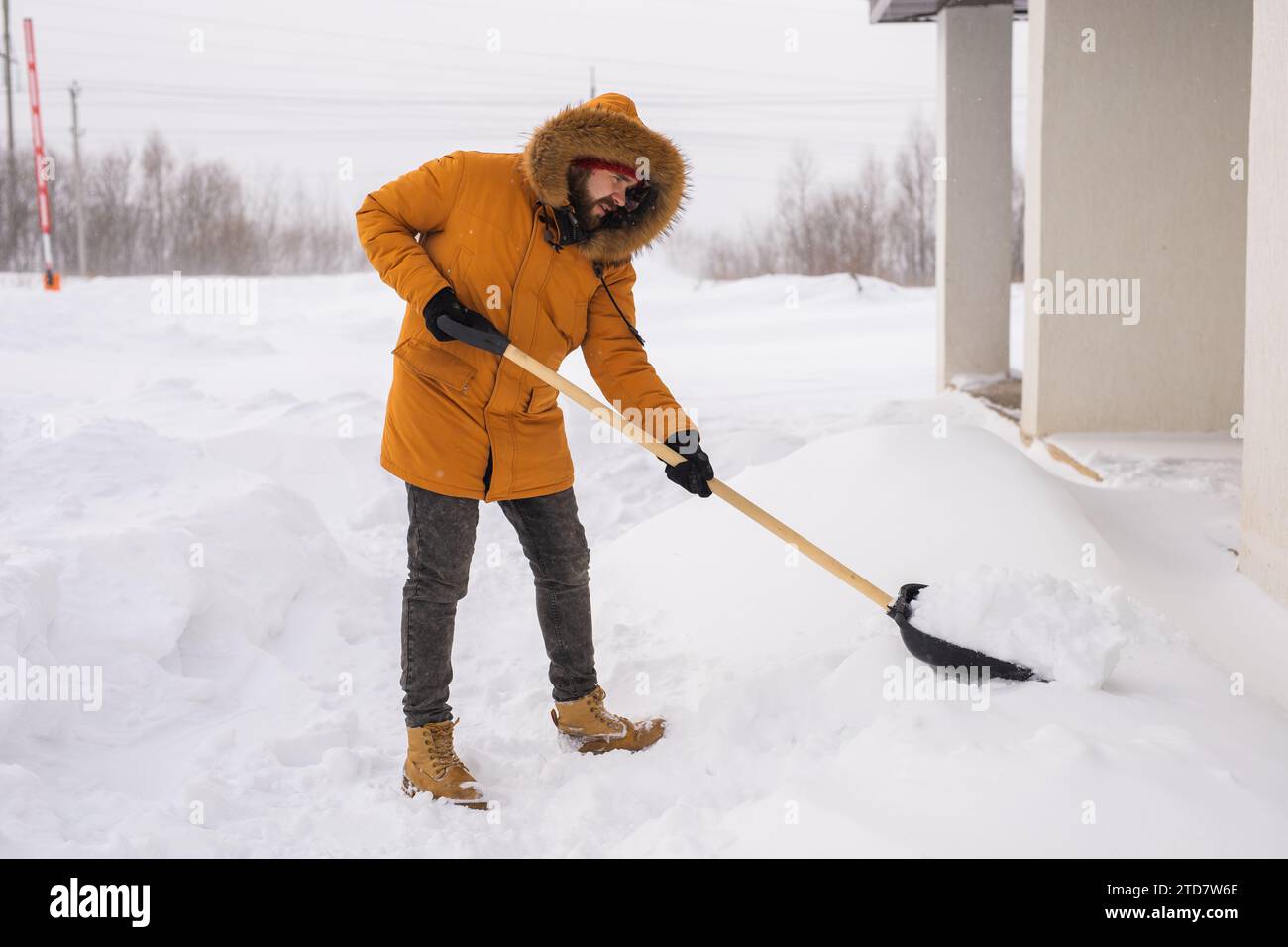 Young man clearing snow in his backyard village house with shovel ...