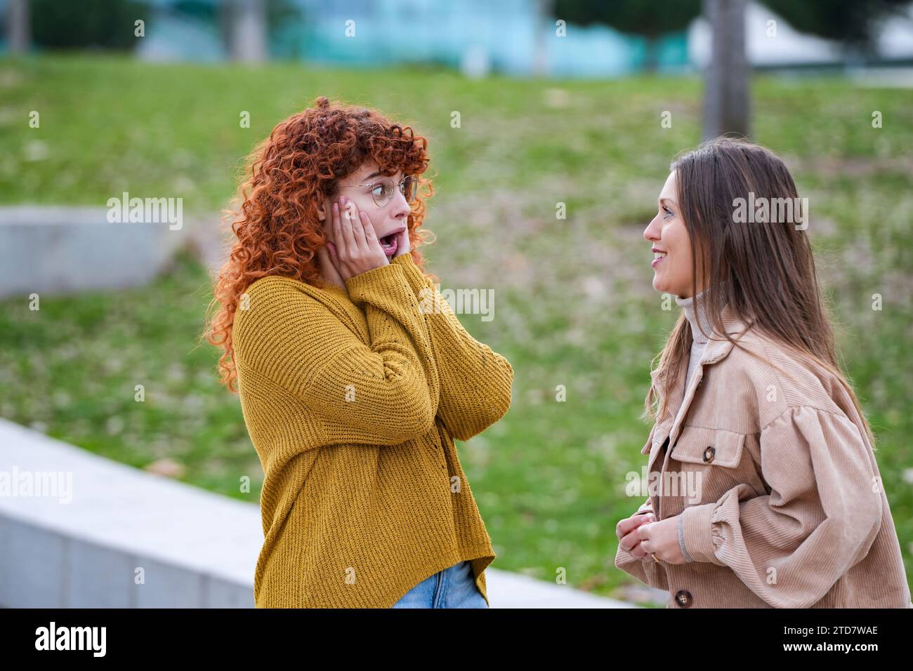 Woman looking surprised at her friend while talking together outdoors ...