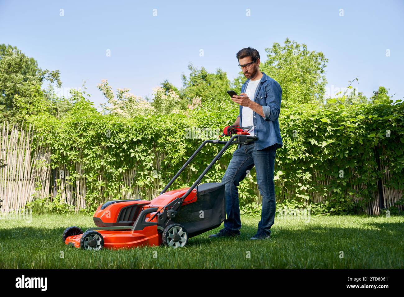 Focused male gardener in glasses using smartphone, while having break ...