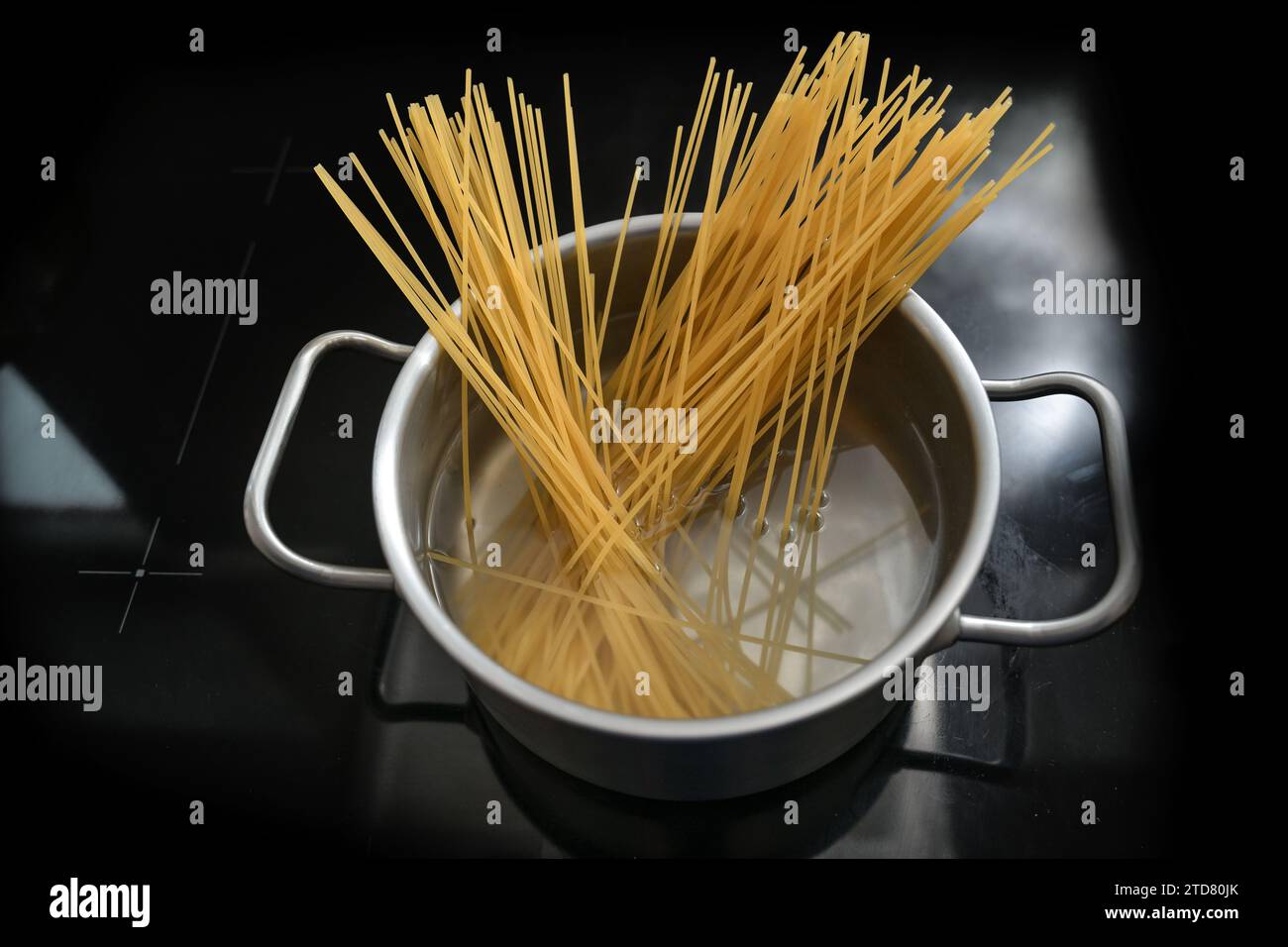 Spaghetti are boiled in a pot of water on a black stove top, cooking ...