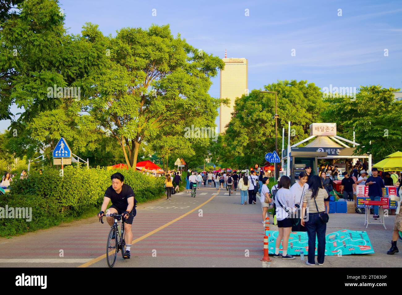 Seoul, South Korea - June 3, 2023: Cyclists ride along a bike path with the iconic 63 Building ...