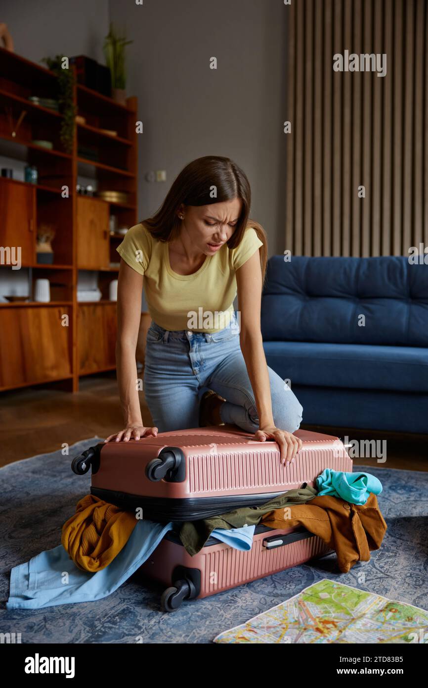 Young woman struggling with overload travel suitcase while preparing ...