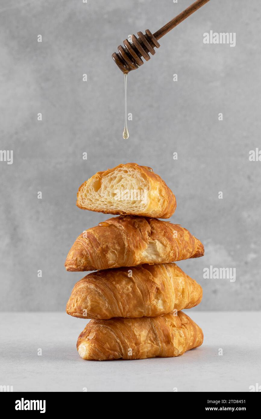 A drop of honey or syrup drips onto a stack of fresh croissants. French ...
