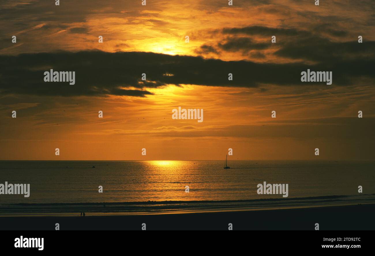 Golden sunset over a calm beach, with calm seas shimmering in hues of ...
