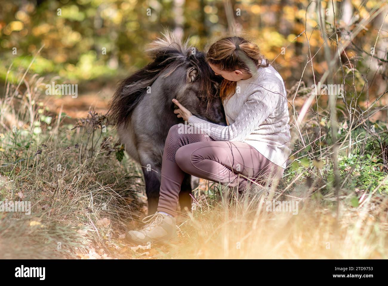A young woman and her shetland pony cuddle together in a forest in ...