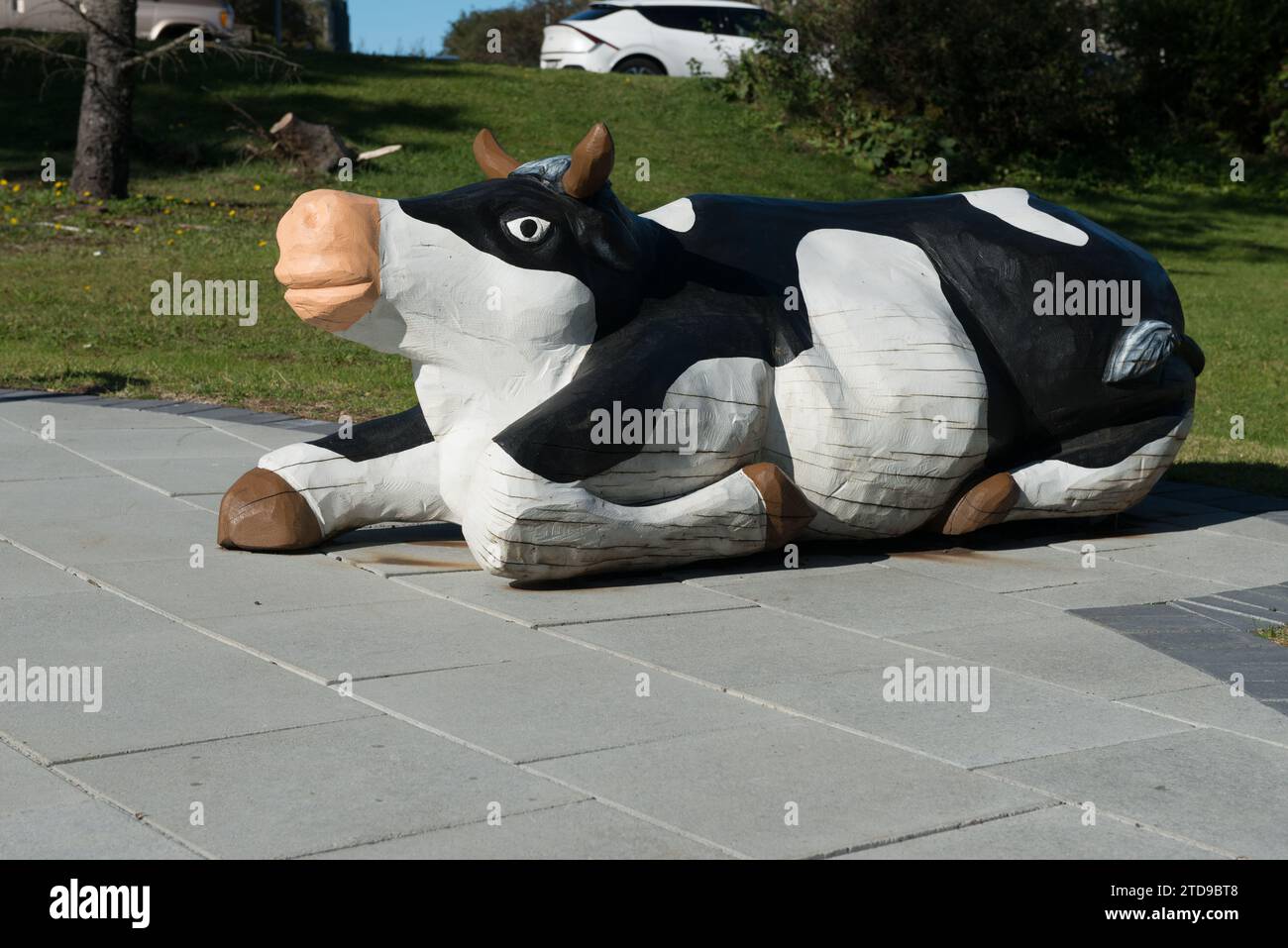 A whimsical sculpture of a black & white cow resting in a park near ...
