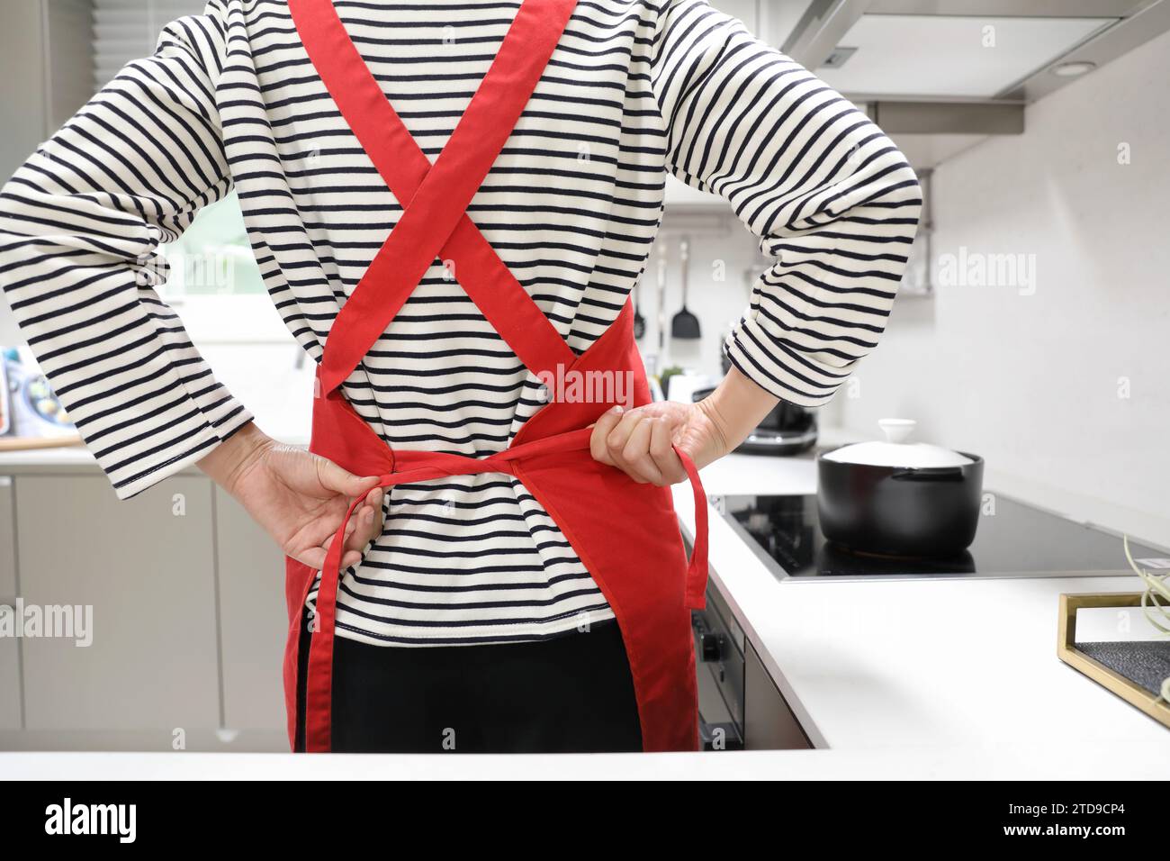 Back view of woman preparing food while tying her apron in the kitchen ...