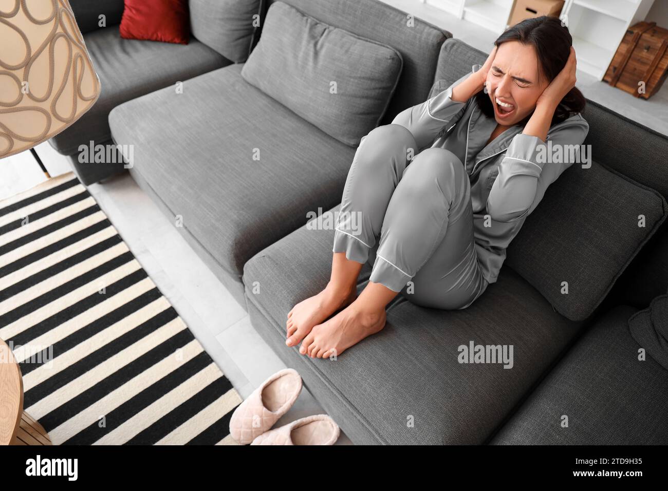 Beautiful young afraid woman sitting on sofa and screaming in living ...